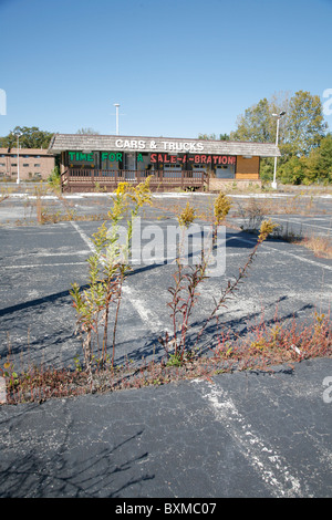 Empty abandoned car and truck dealer lot with weeds growing. Sign reads ...