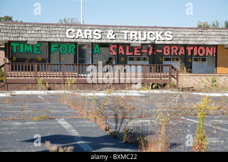 Empty abandoned car and truck dealer lot with weeds growing. Sign reads ...
