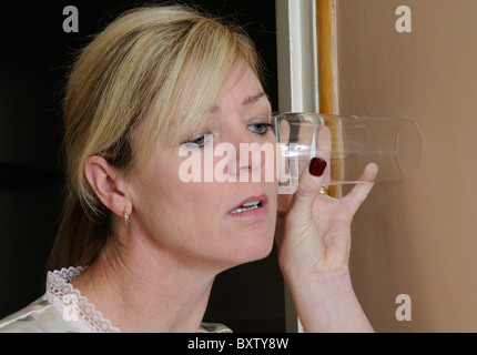 Woman eavesdropper using a glass tumbler to listen through a wall Stock ...