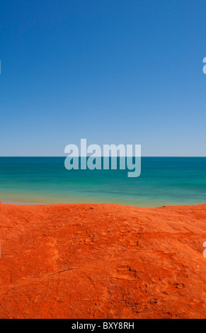 Rocky coastline with red earth, sandy beach and vibrant sky with clouds ...