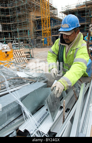 Construction worker loading skip onsite with materials for recycling ...