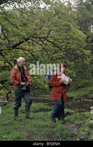 Two elderly people walking ramblers on remote country lane road up a ...