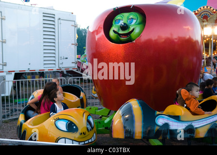 Children ride a kiddy ride at county fair with ferris wheel in Stock ...