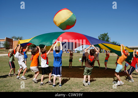 Elementary students use colorful striped tarp or parachute to bounce ...