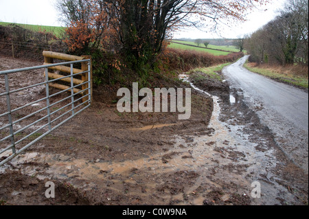 A drainage ditch dug alongside a rural road, carrying muddy water which ...