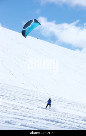 Snowkite riding in the mountains of Utah. Black sail and blue sky above ...
