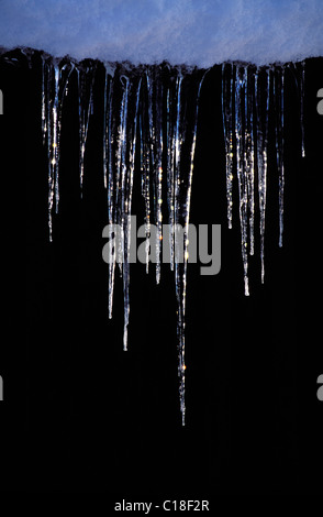 Close-up on ice stalactites formed at the bottom edge of a roof ...