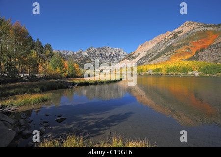 Mountains covered with red and yellow bushes are reflected in the blue ...