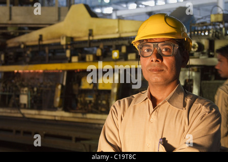Portrait of a male Indian industrial engineer at work holding technical ...
