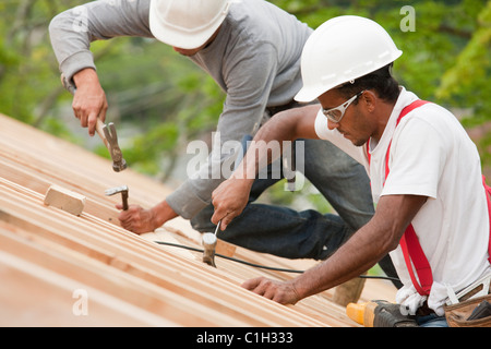 Hispanic carpenters using hammer on deck joist supports Stock Photo - Alamy
