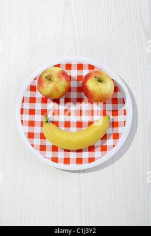 A smiley face made with banana, apple and pears on white background ...