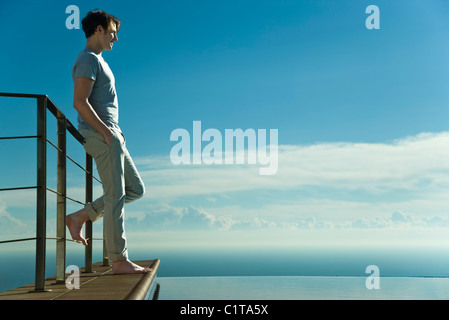Man leaning against railing, looking into distance, low angle view ...
