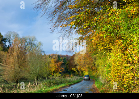 Small saloon car driven along country lane in Autumn, The Cotswolds, UK ...