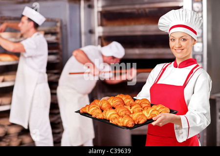 Portrait of baker girl in hat and apron next to display case of fresh ...