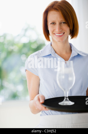 Smiling waitress holding a tray with glass and napkin in a bar or cafe ...