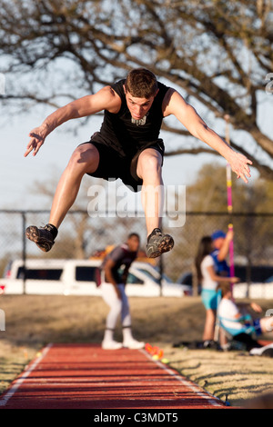 Teenage Anglo male athlete jumps during a long jump competition in ...