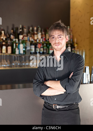 Portrait of bar tender standing with arms crossed at bar counter in ...