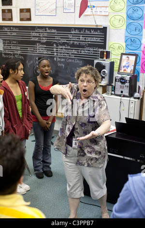 Female teacher singing choir with students holding sheet in classroom ...