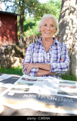Germany, Saxony, Senior woman with newspaper at the farm, smiling ...