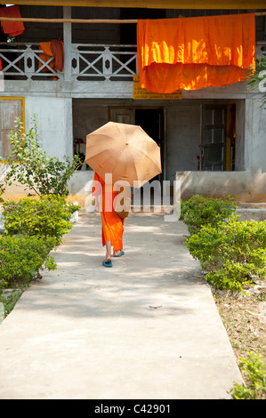 back view of buddhist in orange robe standing near wooden fence in ...