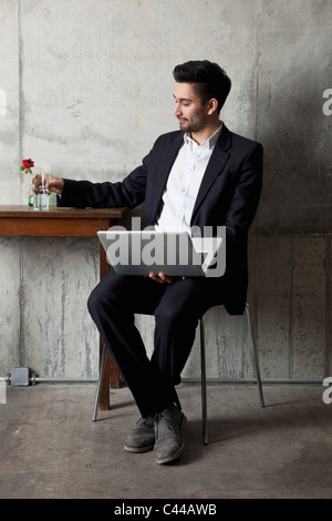 Young businessman with glass of water in hand reading newspaper at ...