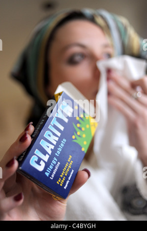 Allergic young woman with tissue and eye drops in park on spring day ...