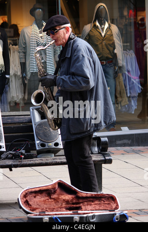 An old man busking on the side of the street beside a bench playing his ...