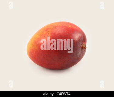 Single ripe mango with golden yellow skin resting on light textured ...