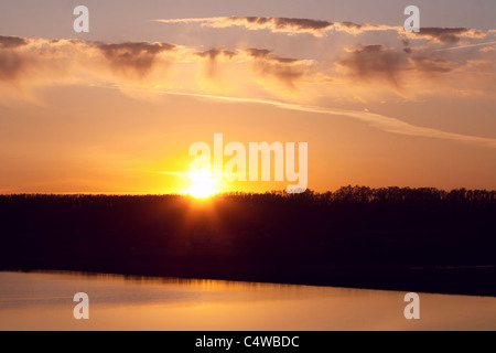 Red sunrise sunset over a tree line horizon with heavy orange clouds ...