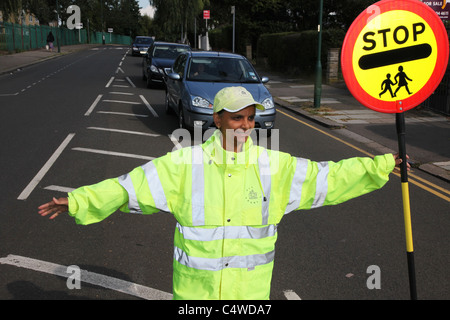 A lollipop lady stops traffic to help school children across the road ...