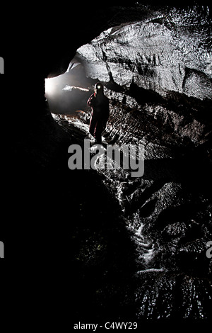 Silhouette of caver in cave passage with waterfall Ogof Draenen Wales ...