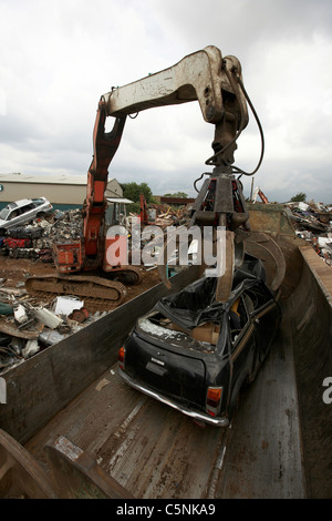 Crane lifting scrap car into a car crusher for recycling in a scrapyard ...