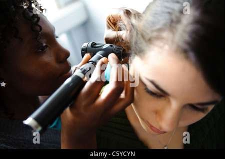 Female audiology and deafness student looking into the ear of another ...