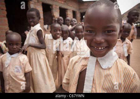 group of young Ugandan school children in smart uniforms sit on wooden ...