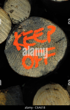 Warning sign "Keep Off Log Stacks" on a log pile in woodland where ...