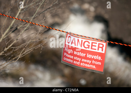 Danger sign along dangerous flood water in stream, creek and river ...