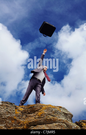 Businessman throwing briefcase off cliff Stock Photo - Alamy