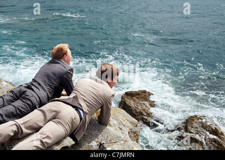 Businessmen peering over cliff edge Stock Photo - Alamy