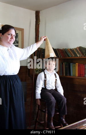A young boy sitting wearing a DUNCE hat in a historic schoolroom Stock ...