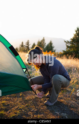 brunette woman setting up a tent in a forest with a hat on her head ...