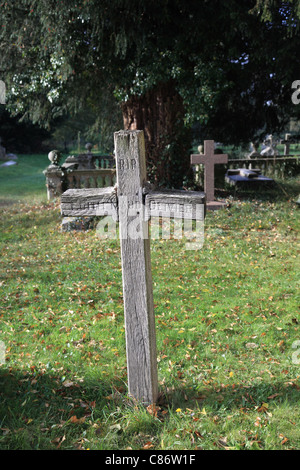 Weathered wooden cross and grave stone standing in an old settlers graveyard in a dense forest ...