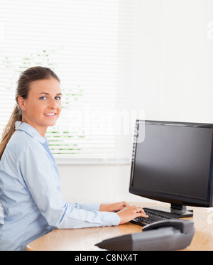 Young woman typing on keyboard while touching glasses at temple beside ...