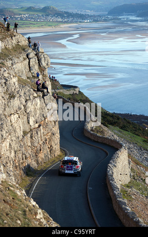 People watch from the hillside as a rally car rounds a corner during a ...