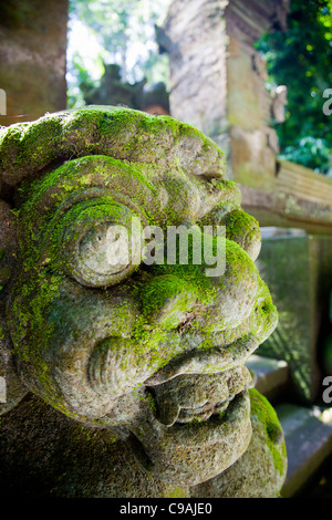 Stone carved Balinese statue covered by musk trees in the background ...