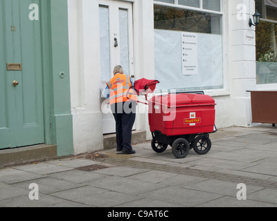 A female Royal Mail postal worker with trolley delivering post to a ...