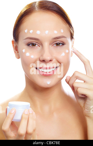 Beautiful woman applying cream onto her face on light green background ...