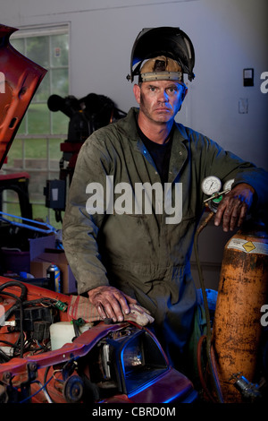 A grease covered blue collar working man takes a break, looking ...