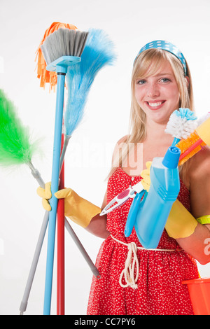 Young woman with cleaning supplies in shopping cart on red background ...