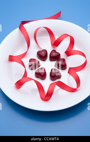 Heart-shaped plate with chocolate candies and rose flowers on turquoise ...
