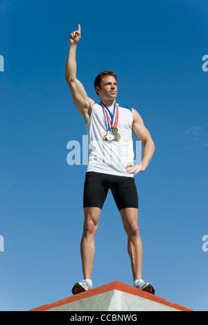 Male athlete standing on winner's podium with arms raised in victory ...